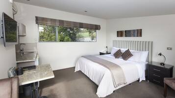 Quarto com cama, mesas de cabeceira, escrivaninha e janela com vista para o verde.