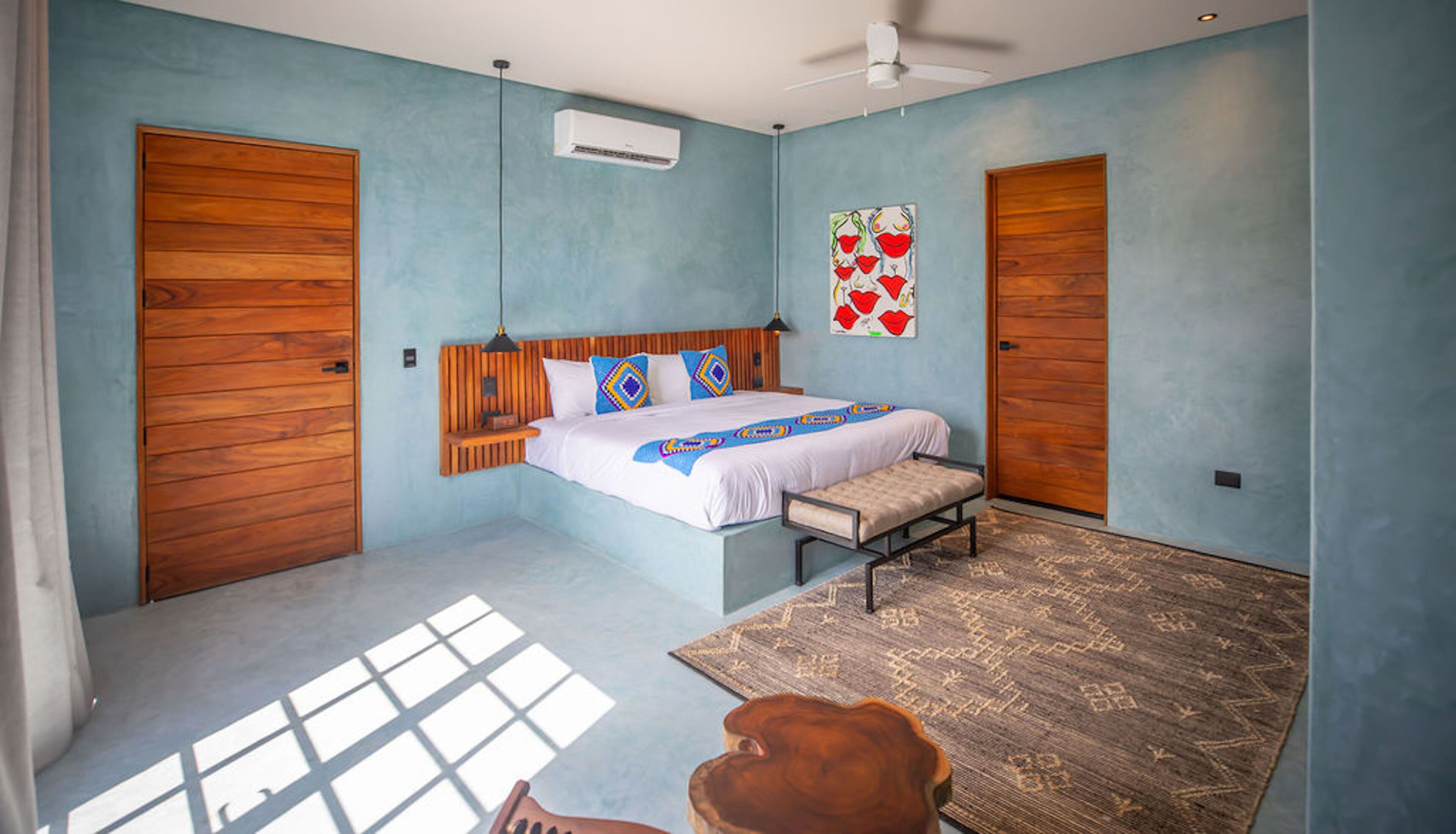 Um quarto com cama, um banquinho, um tapete e um ventilador de teto.