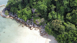 Uma área costeira com costa rochosa, floresta verde densa e água turquesa cristalina.