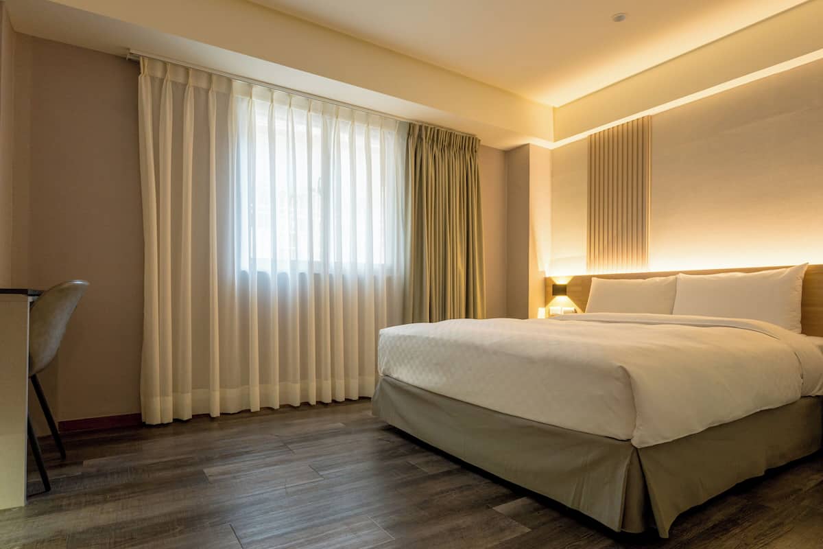 Quarto de hotel com uma cama grande, uma escrivaninha e uma janela com cortinas.