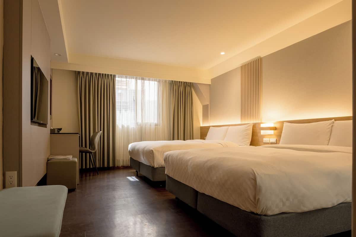 Quarto de hotel com duas camas, uma escrivaninha, uma cadeira e uma televisão.