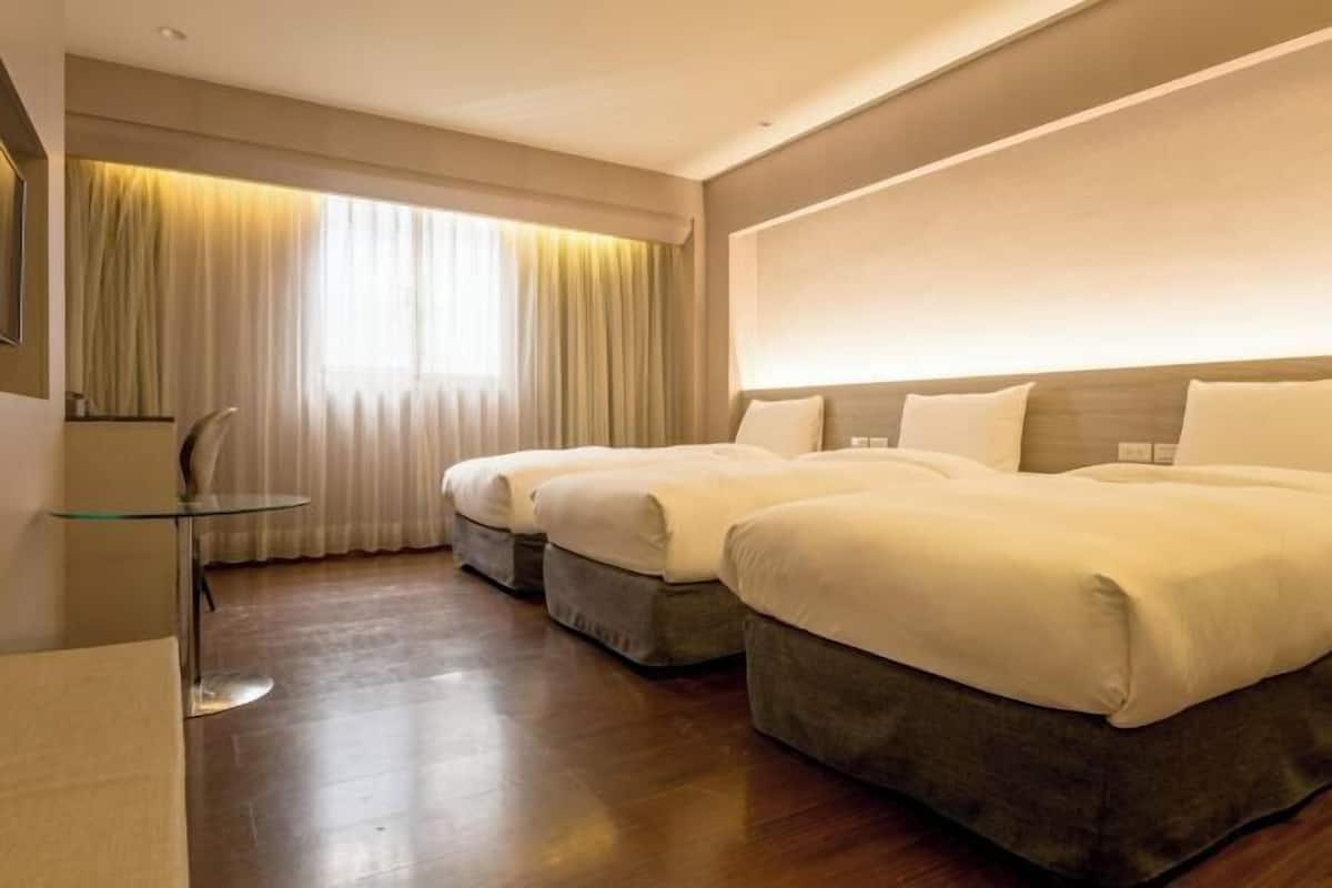 Quarto de hotel com duas camas, uma mesa de vidro e uma janela grande com cortinas.