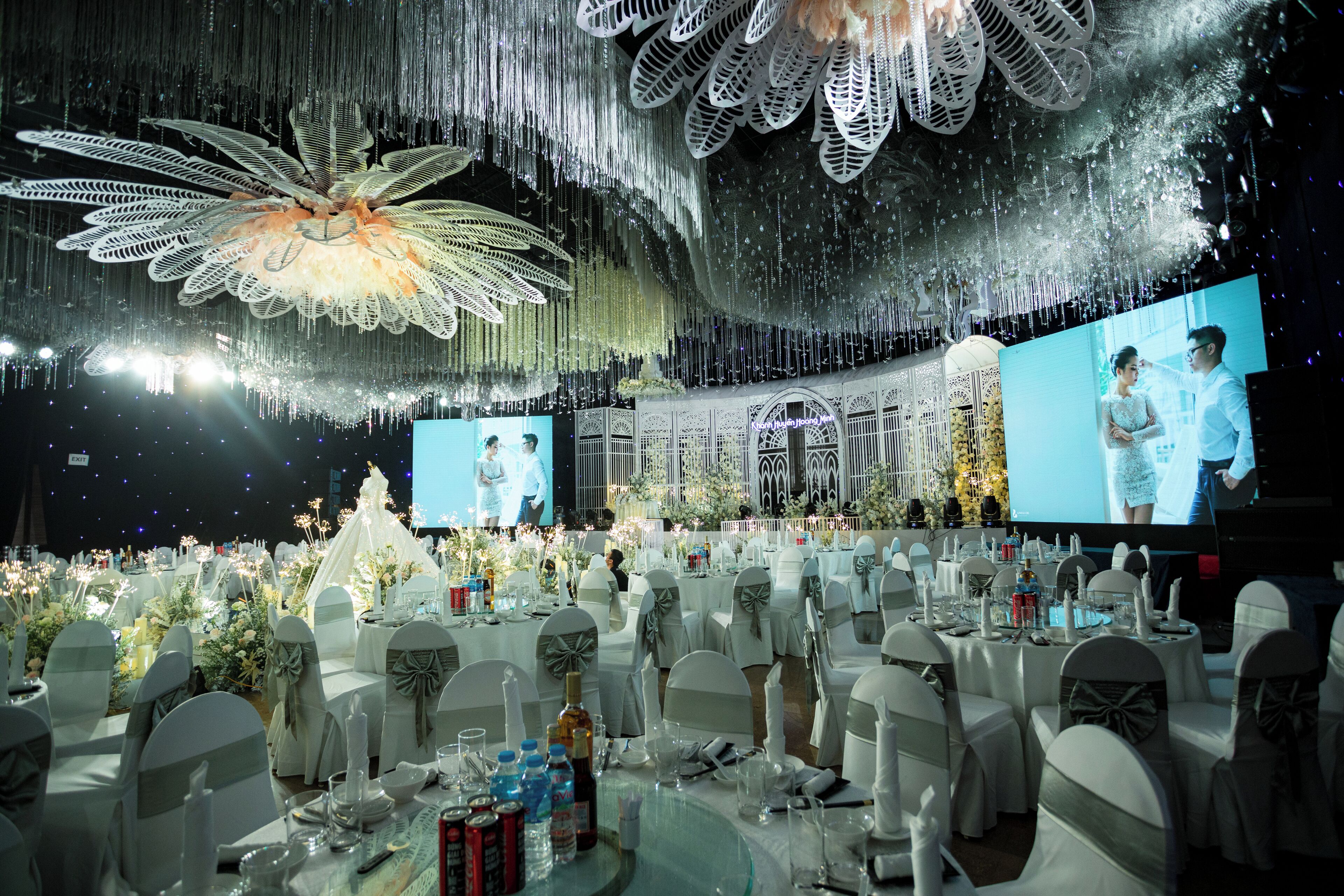 Salão de banquetes com mesas redondas, cadeiras brancas e decorações penduradas.