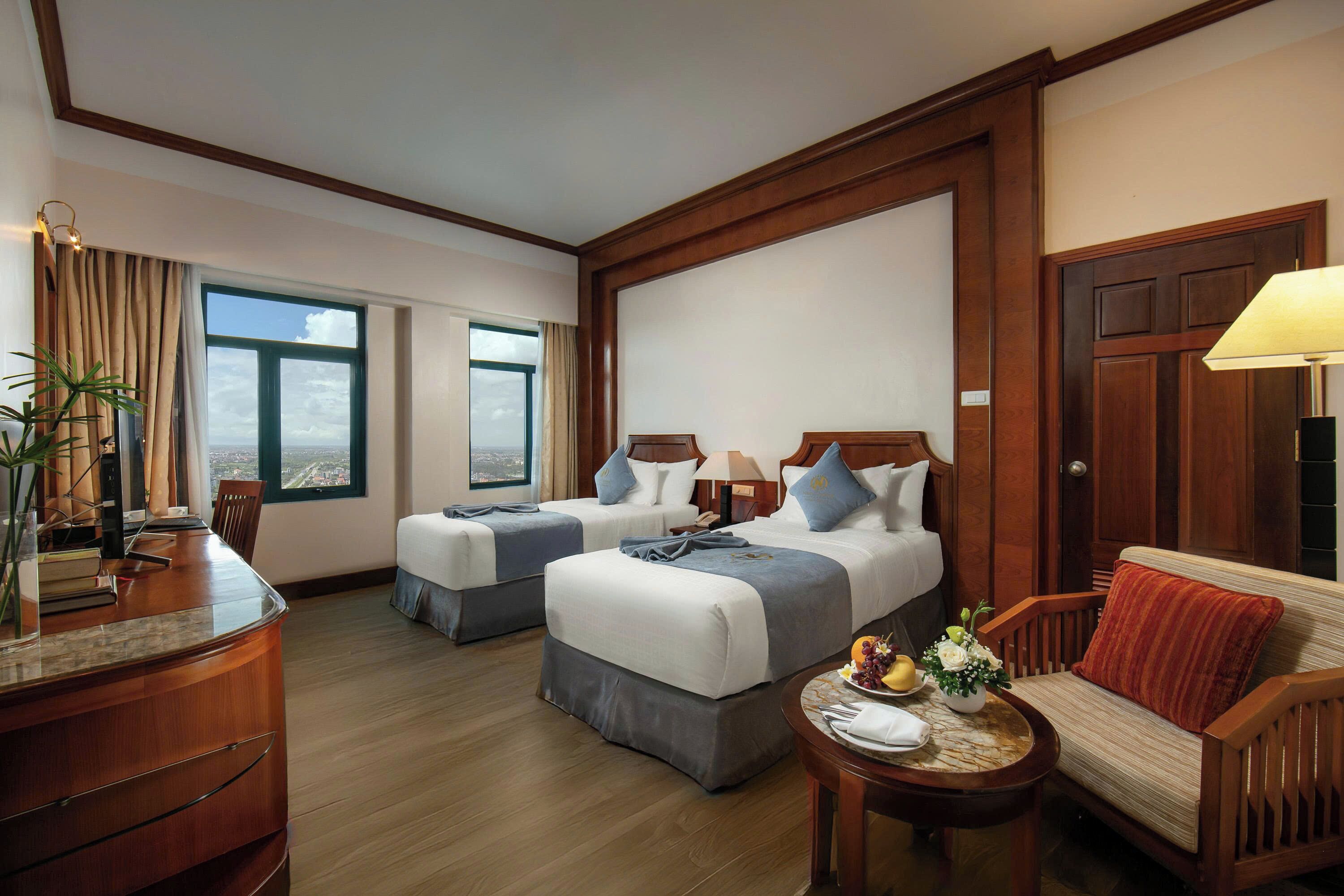 Quarto de hotel com duas camas, uma escrivaninha, uma cadeira e vista para a cidade.
