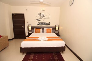 Quarto de hotel com cama, mesa de cabeceira, relógio na parede e porta.