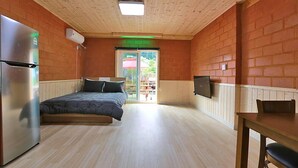 Quarto com cama, geladeira, teto de madeira e vista para o exterior.