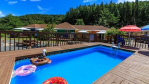 Piscina com deck de madeira, cercada por uma vedação de madeira, e um morro coberto de vegetação ao fundo.