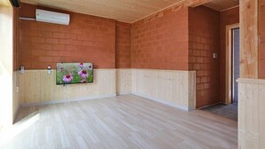 Quarto com piso de madeira, televisão fixada na parede e parede de tijolos.