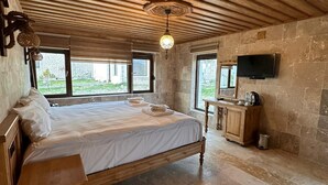 Um quarto espaçoso com uma cama grande, teto de madeira, paredes de pedra, televisão e vista para o exterior.