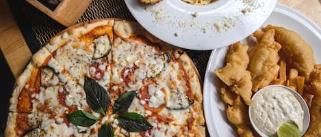 Pizza com diversos ingredientes, um prato de peixe frito e uma tigela de molho.