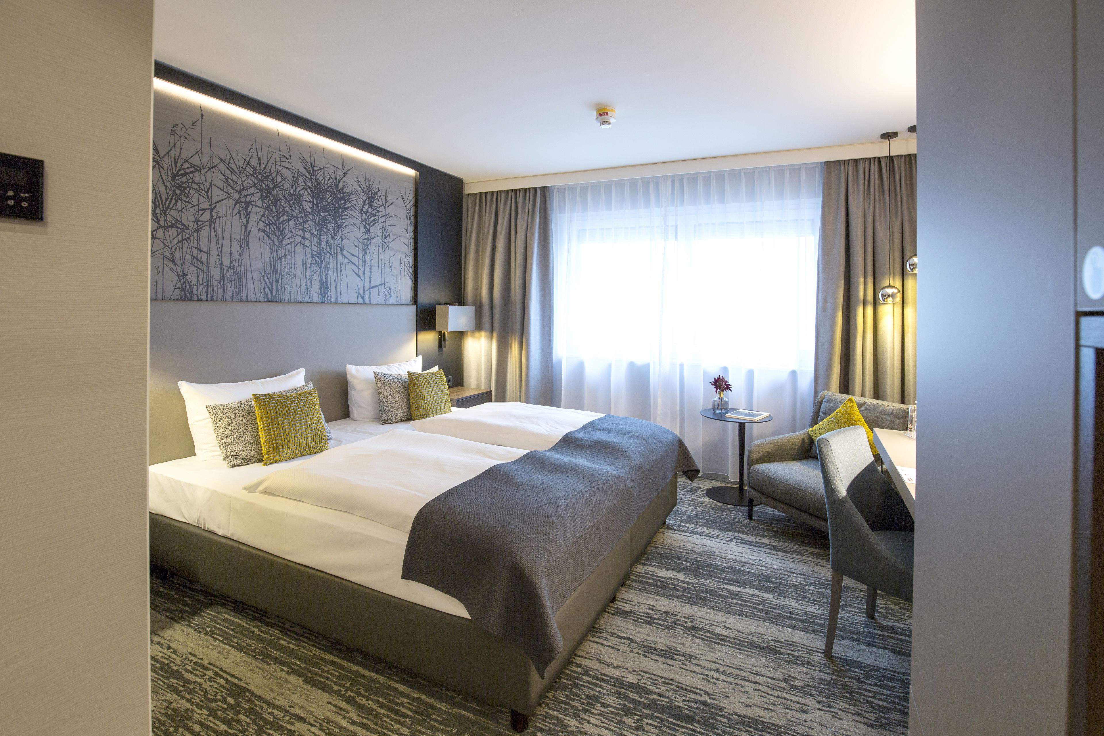 Quarto de hotel moderno com uma cama grande, um sofá, uma mesinha e uma obra de arte na parede.