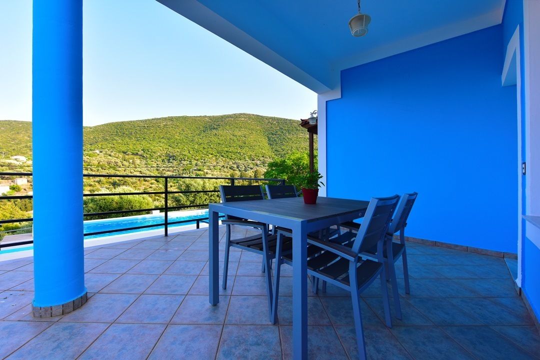 Terraço com mesa e cadeiras, um vaso de planta e vista para uma piscina e colinas.