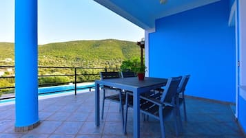 Terraço com mesa e cadeiras, um vaso de planta e vista para uma piscina e colinas.