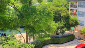 Uma área residencial com um edifício de dois andares, uma varanda e vista para uma rua arborizada.