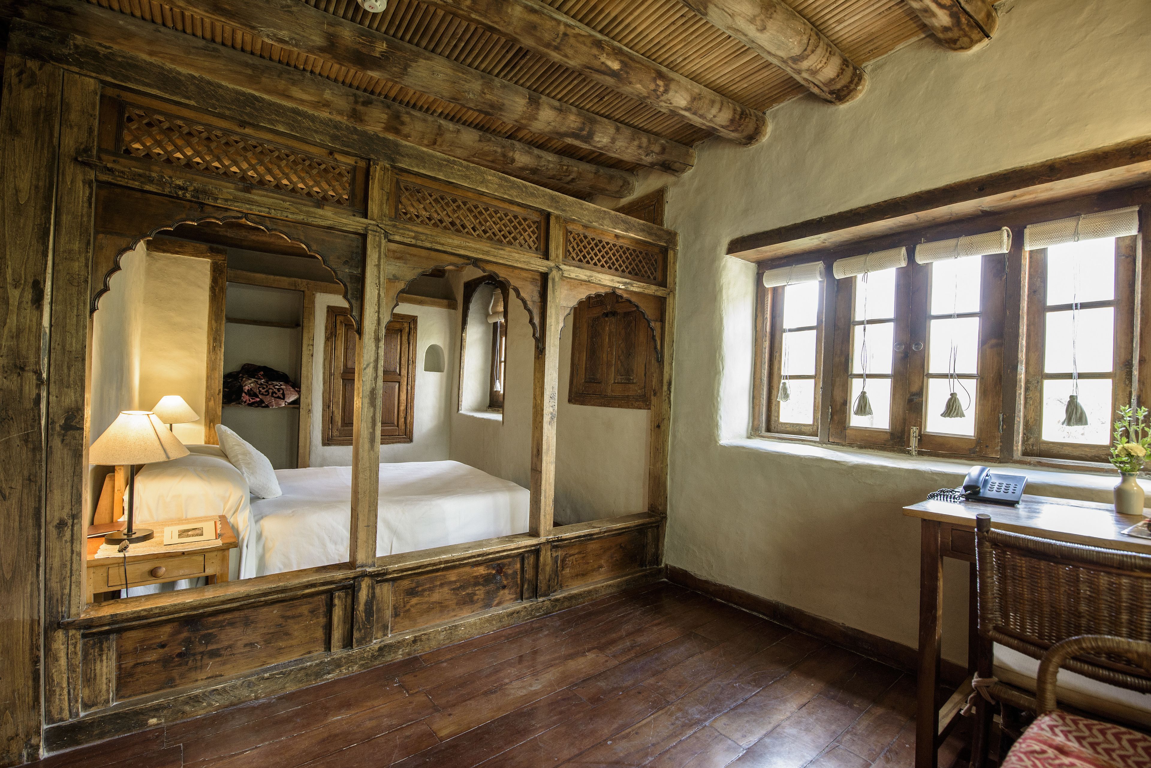 Quarto tradicional com uma cama de madeira, uma mesa com telefone e uma janela com cortinas.