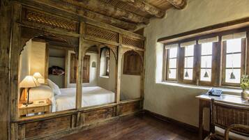Quarto tradicional com uma cama de madeira, uma mesa com telefone e uma janela com cortinas.