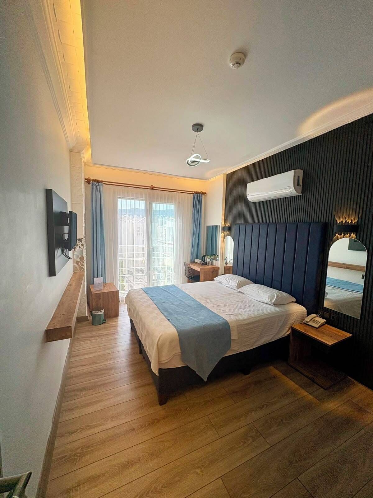 Quarto de hotel moderno com uma cama grande, uma mesa de cabeceira, um espelho e um ar condicionado fixado na parede.