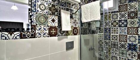 Casa de banho com lavatório, sanita e zona de duche. As paredes estão decoradas com azulejos estampados.