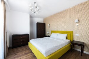 Quarto com cama amarela, cómoda de madeira e papel de parede estampado.