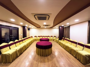 Sala de conferência com uma mesa comprida e cadeiras, piso de madeira e teto com iluminação embutida.