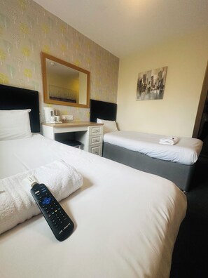 Quarto de hotel com duas camas, uma escrivaninha com espelho, um controle remoto e uma parede com papel de parede estampado.