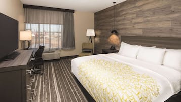 Quarto de hotel com cama, escrivaninha, cadeira, luminária e vista da cidade pela janela.