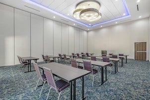 Sala de conferências com mesas e cadeiras, um tapete estampado e uma luminária moderna no teto.