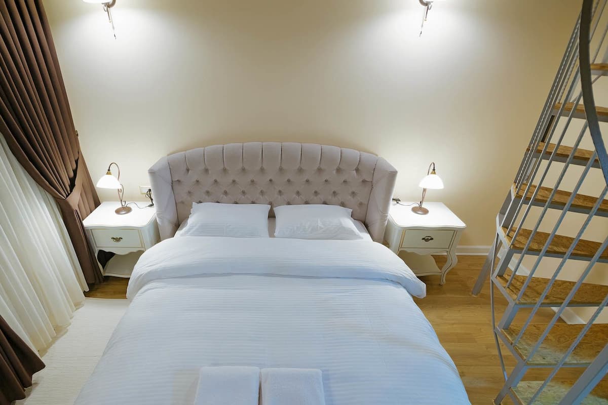 Uma cama bem arrumada com lençóis brancos, duas mesas de cabeceira com abajures e uma cabeceira com design acolchoado.