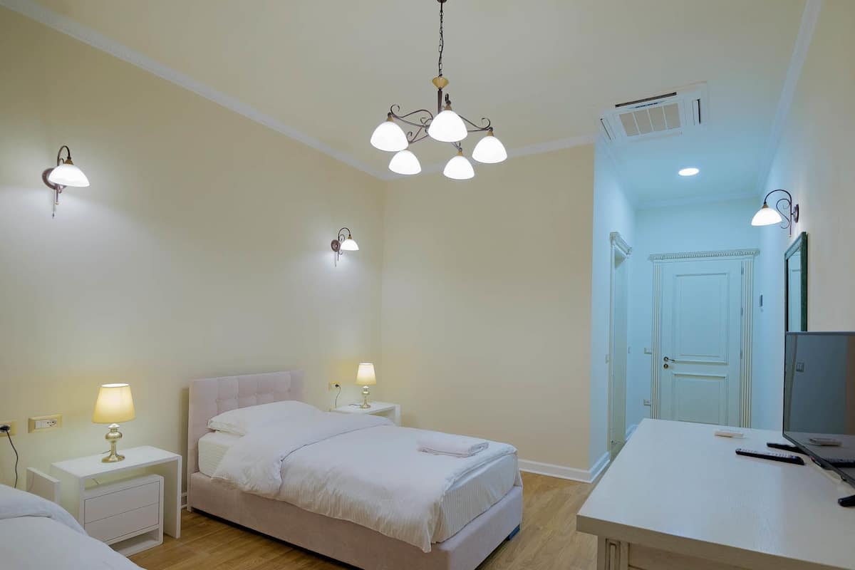 Quarto com cama, mesas de cabeceira com luminárias, televisão e luminária no teto.