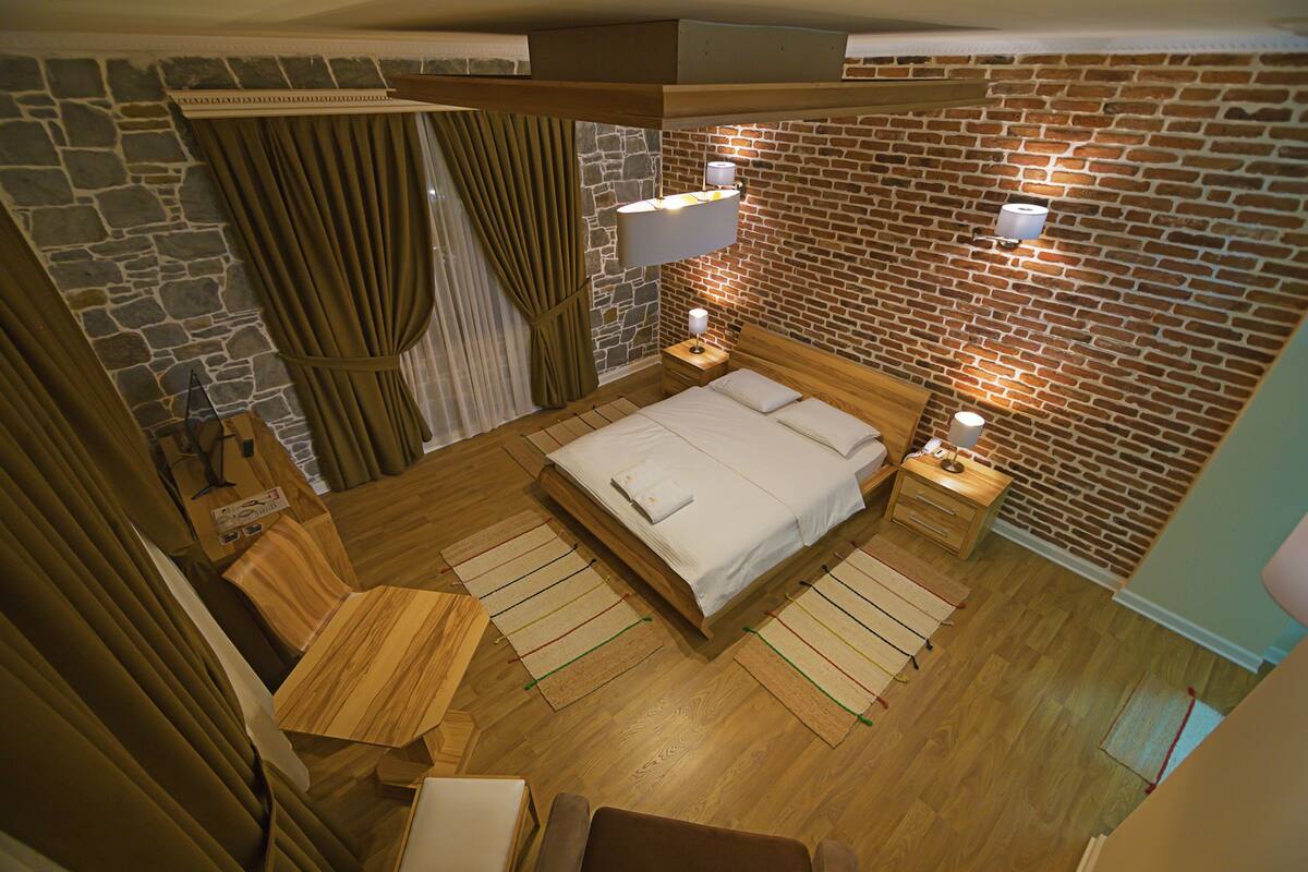 Quarto com parede de tijolos, móveis de madeira, cama com roupa de cama branca e uma pequena mesa.