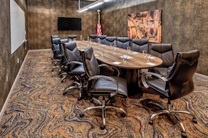 Uma sala de conferências com uma grande mesa oval, cadeiras de couro preto, uma bandeira e um quadro na parede.