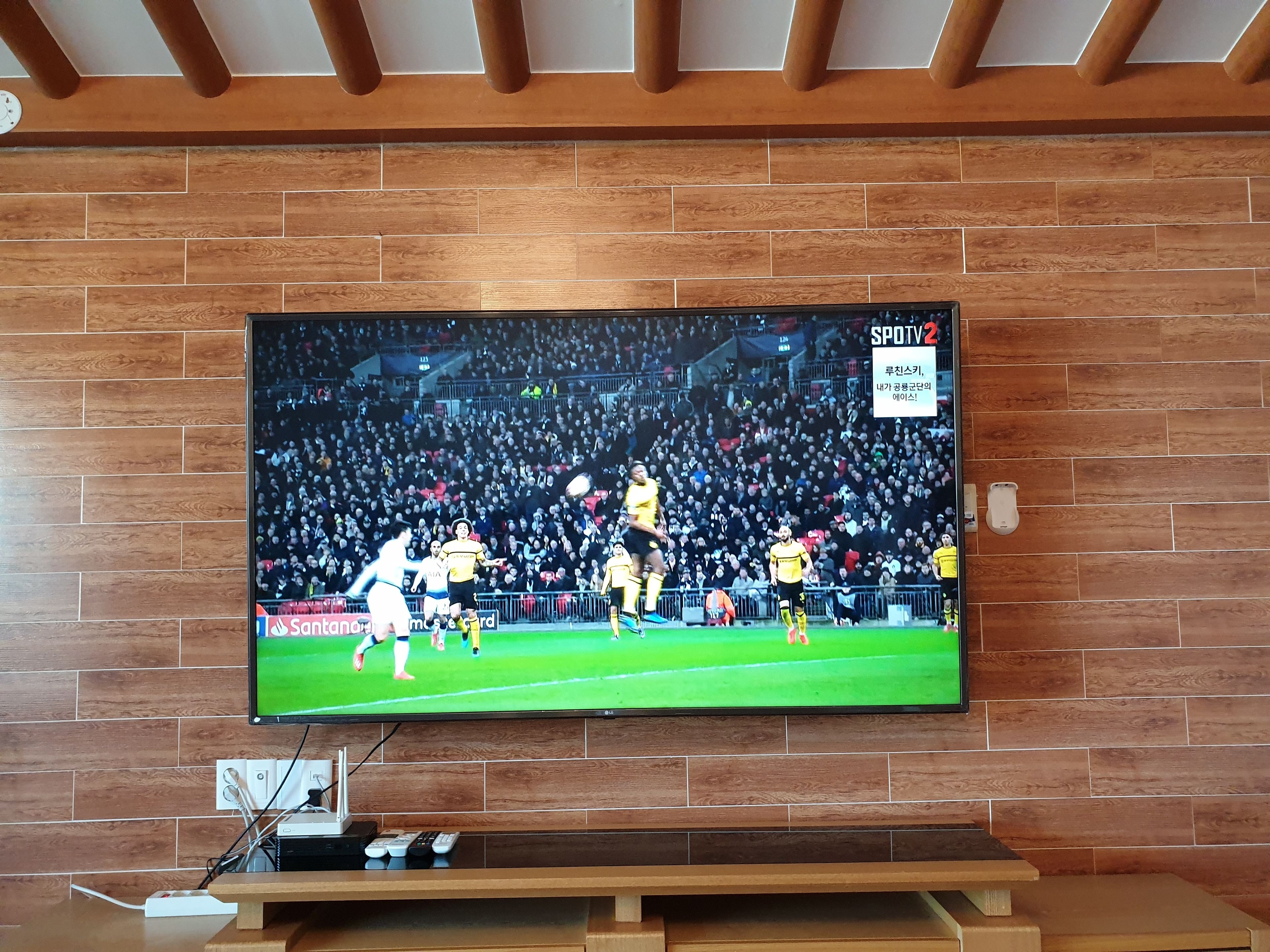 Televisão presa a parede de madeira exibindo uma partida de futebol.
