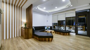 Um interior moderno com piso de madeira, um sofá seccional preto, uma mesa de centro de madeira e uma janela grande com persianas.
