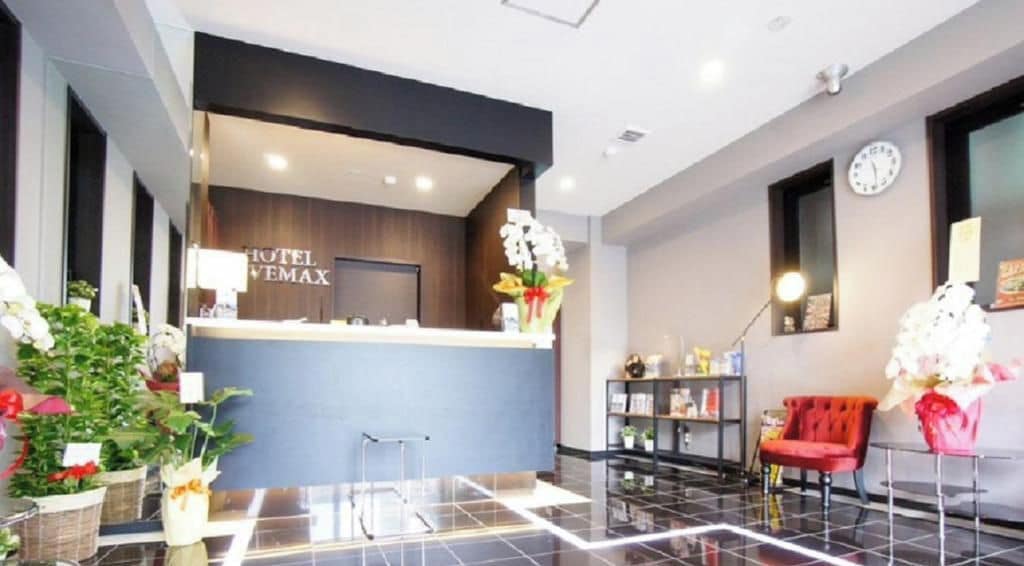 Área de recepção de hotel com balcão, relógio e uma cadeira vermelha.