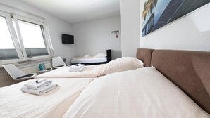 Quarto de hotel com duas camas, uma escrivaninha, uma cadeira, uma televisão e uma janela com persianas.