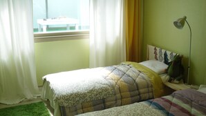 Quarto com duas camas, janela com cortinas, luminária e parede verde.