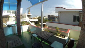 Varanda com mesa e cadeiras, antena parabólica e vista dos edifícios ao redor.