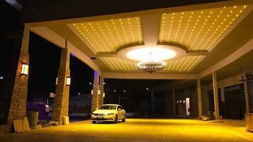 Área externa coberta com um carro estacionado sob uma marquise com um candelabro.