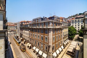 Um edifício histórico com vários andares, janelas amplas e um bondinho passando na frente.