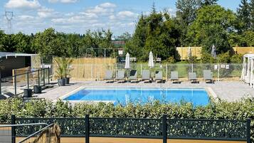 Piscina retangular com espreguiçadeiras e guarda-sóis, rodeada por uma cerca e vegetação.