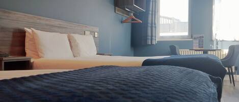 Quarto de hotel com uma cama grande, mesa de cabeceira, televisão na parede e janela com cortinas.