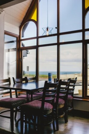 Uma área de refeições com mesa, cadeiras, janelas amplas e vista para o exterior.