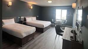 Quarto de hotel com duas camas, uma escrivaninha, uma cadeira, uma televisão e uma janela.