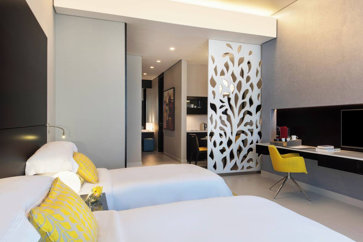 Quarto de hotel moderno com duas camas, uma escrivaninha, uma cadeira e uma televisão.