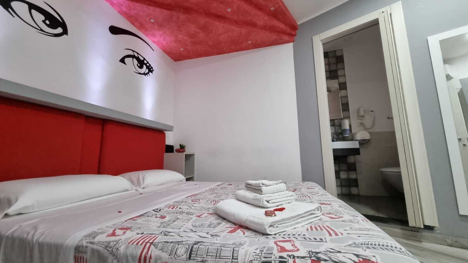 Uma cama bem arrumada com colcha estampada, cabeceira vermelha e parede com um desenho de olho grande.