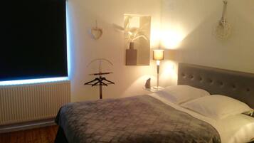 Quarto bem arrumado com uma cama, abajures, radiador, decoração de coração na parede e uma janela com persianas.