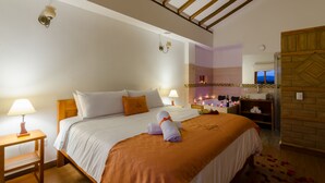 Quarto de hotel com cama, abajures, cabeceira de madeira, mesa de cabeceira, banheiro com espelho e guarda-roupa de madeira.