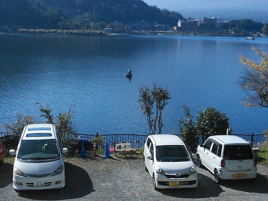 Uma área de estacionamento com três carros brancos, um lago e uma montanha ao fundo.