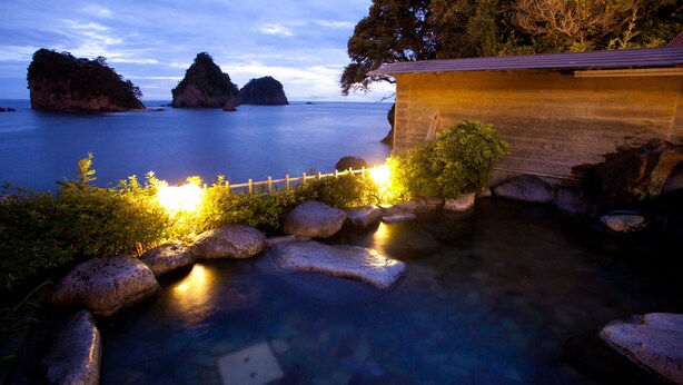 Cena costeira tranquila com um edifício de madeira, águas claras e formações rochosas.