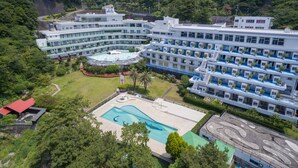 Um hotel moderno com vários andares, piscina e vegetação exuberante ao redor da propriedade.